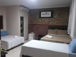 Quarto de hotel com duas camas, uma pequena mesa, um frigorífico e uma parede de pedra.