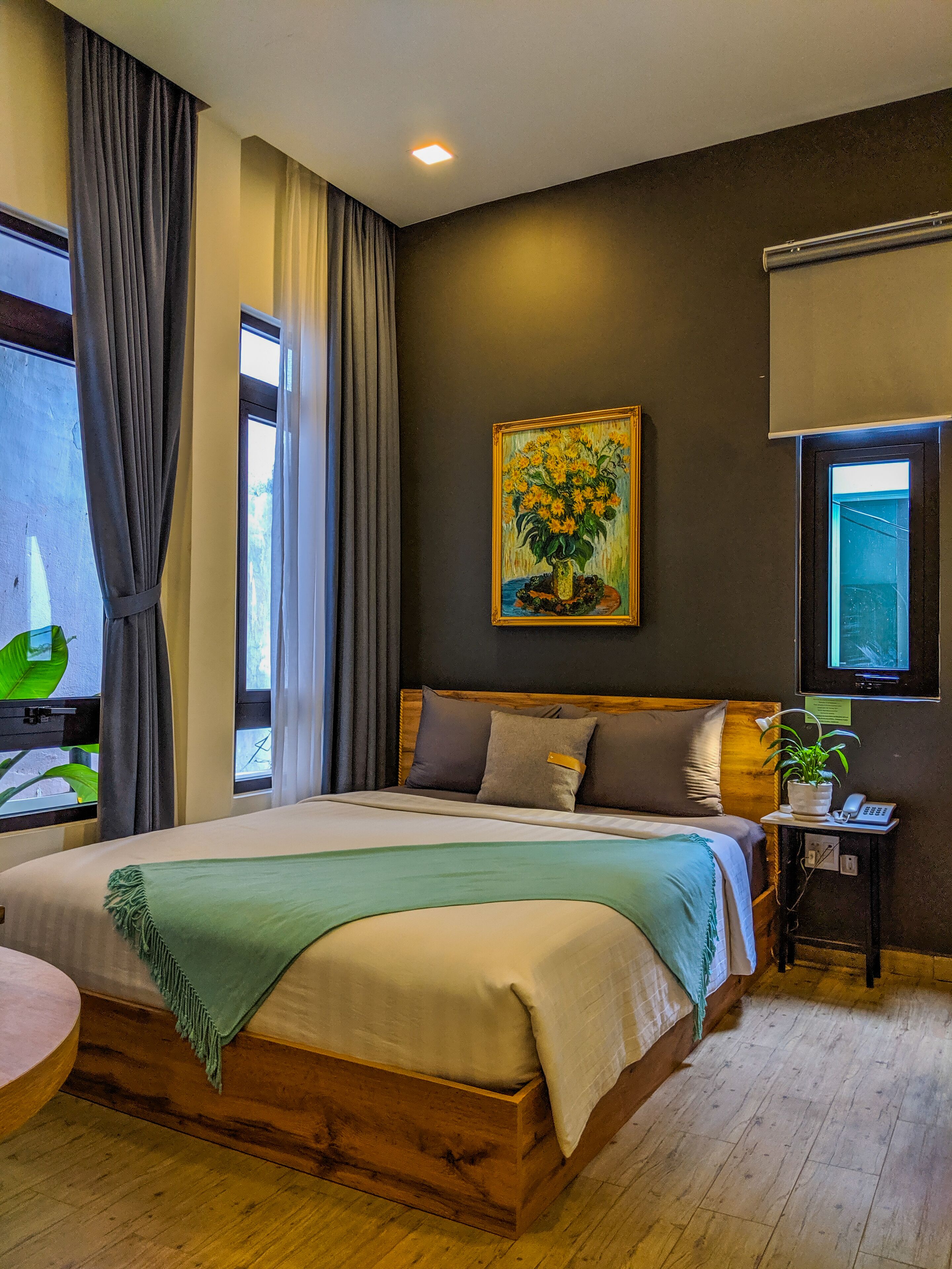 Quarto moderno com cama de madeira, pintura de flores na parede e mesa de cabeceira com planta e telefone.