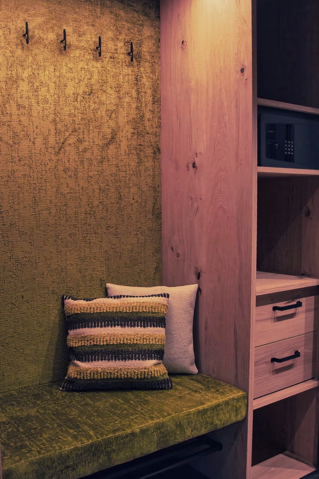 Um quarto com um banco estofado verde, um guarda-roupa de madeira e um rádio fixado na parede.