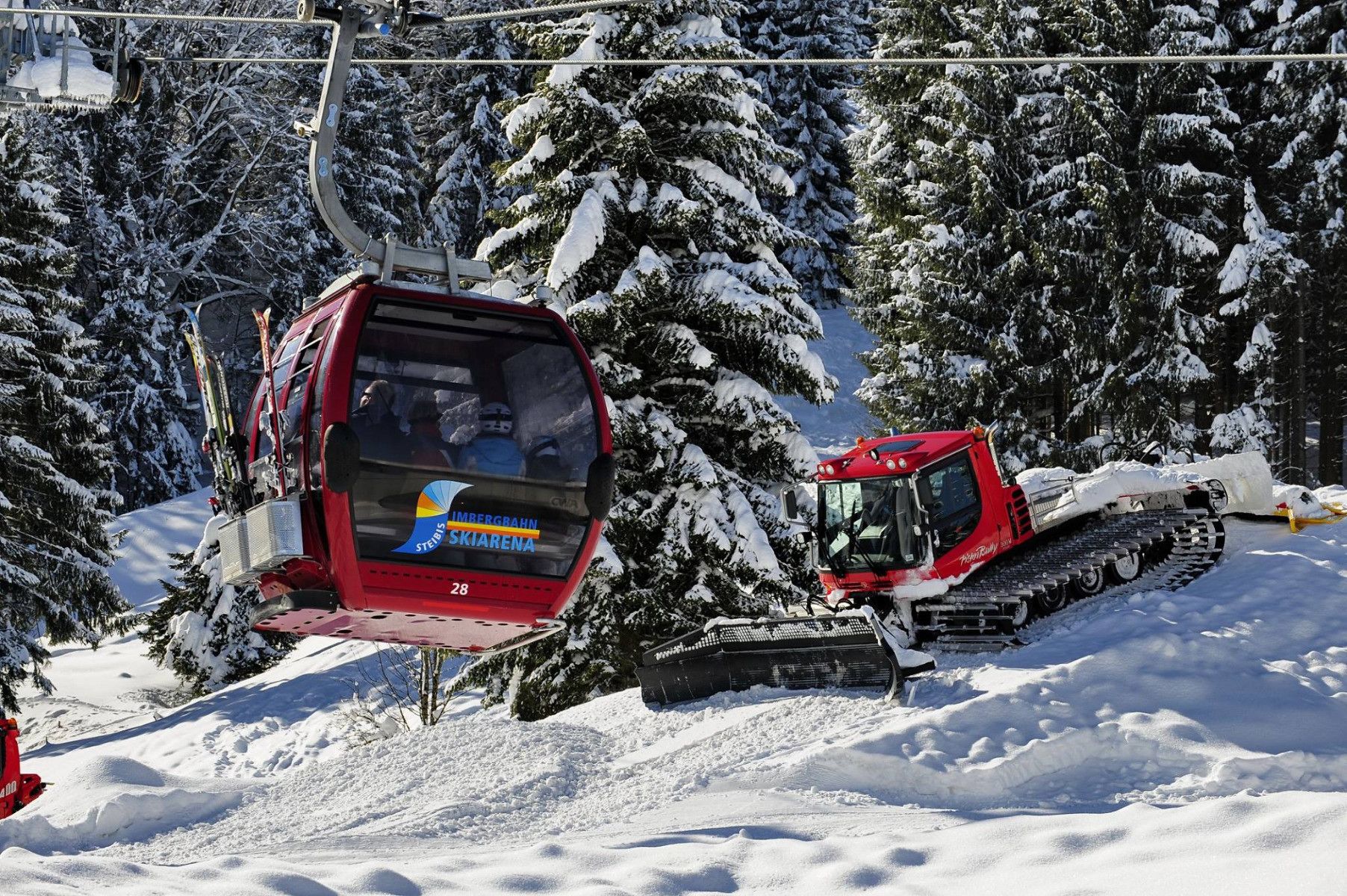 Uma cadeira de teleférico com esquis, uma máquina de preparação de neve vermelha e árvores cobertas de neve.