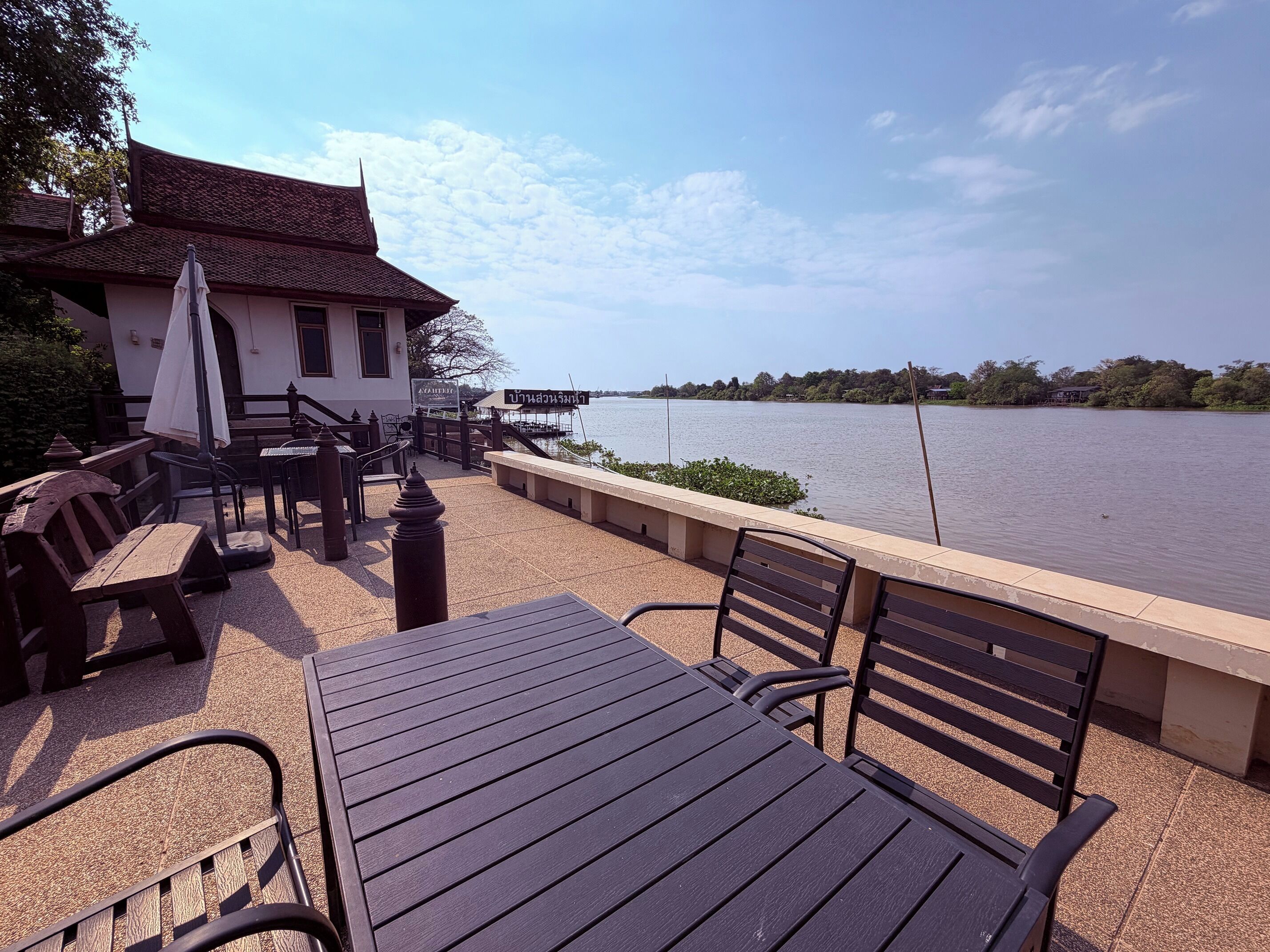 Terraço com mesa e cadeiras, com vista para águas calmas e uma linha de costa distante.