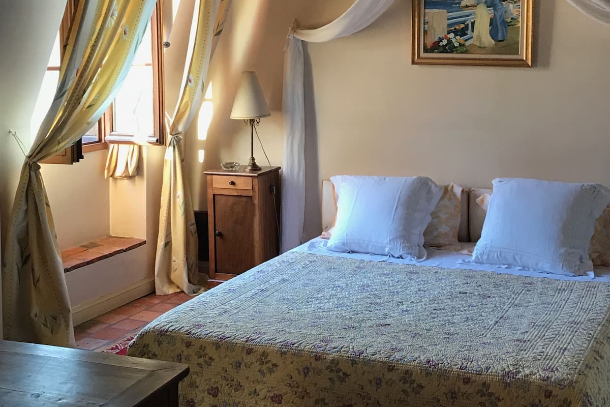 Quarto com cama, mesa de cabeceira, abajur e um quadro na parede.