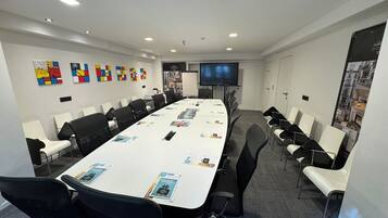 Uma sala de conferências com uma mesa comprida, cadeiras, uma tela e obras de arte coloridas nas paredes.