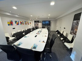 Uma sala de conferências com uma mesa comprida, cadeiras, uma tela e obras de arte coloridas nas paredes.