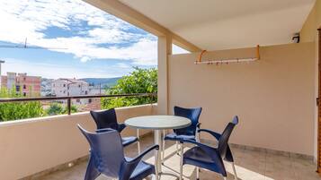 Varanda com uma mesa redonda e quatro cadeiras, com vista para uma área residencial com casas e vegetação.