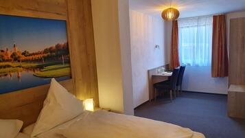 Quarto de hotel com cama, escrivaninha e cadeiras, quadro na parede e janela com cortinas.