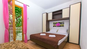 Quarto com uma cama, uma mesinha, uma janela com uma imagem e uma porta deslizante com cortinas rosa.