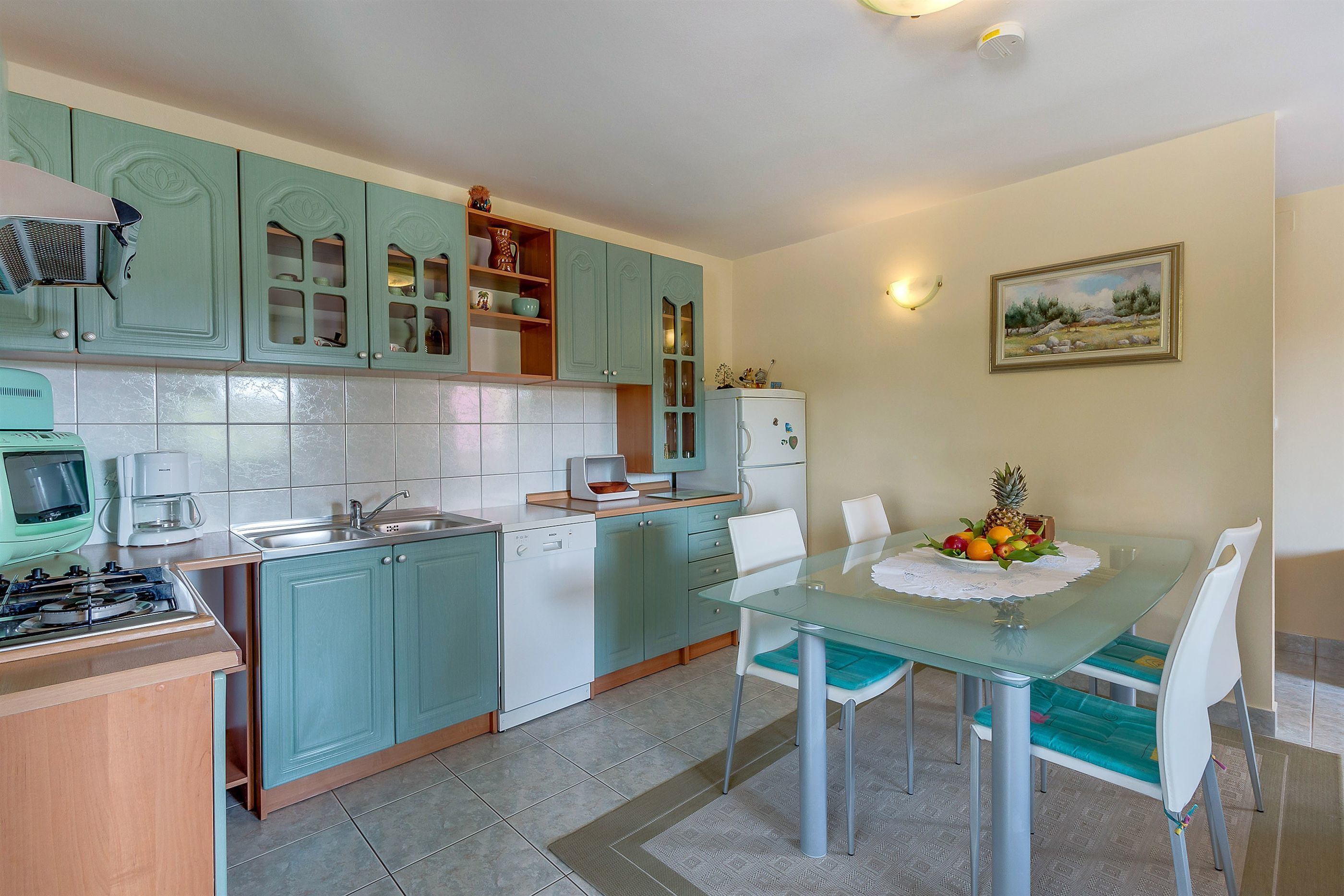 Uma cozinha compacta com armários verde-água, uma mesa de jantar com cadeiras e uma geladeira.