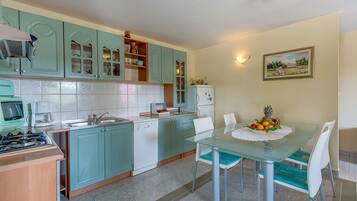Uma cozinha compacta com armários verde-água, uma mesa de jantar com cadeiras e uma geladeira.