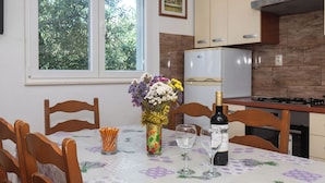 Uma mesa de jantar com cadeiras, um vaso de flores, copos de vinho e uma garrafa de vinho.