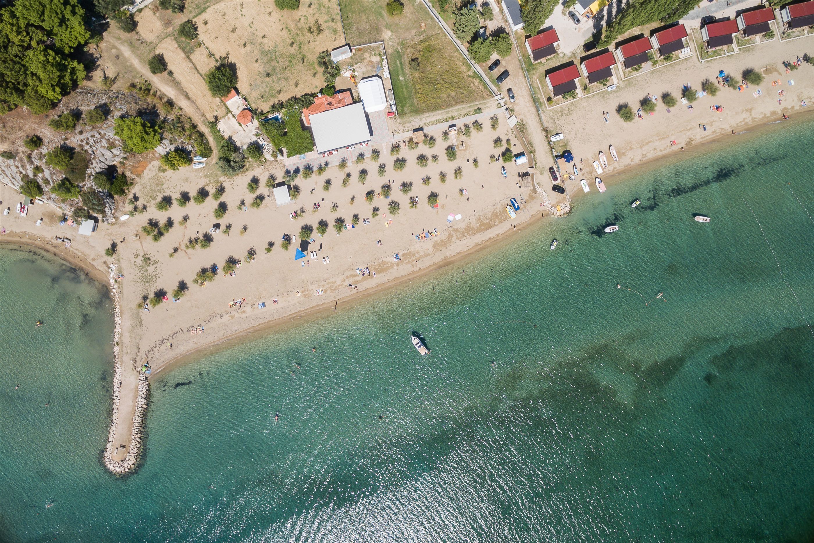 Vista aérea de uma área costeira com praia, uma fileira de edifícios e vários barcos na água.