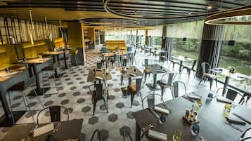 Um restaurante com piso de padrão hexagonal, móveis modernos e grandes janelas com vista para um rio.