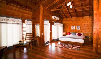 Um quarto tipo cabana de madeira, com uma cama, uma mesa com um vaso e cortinas.