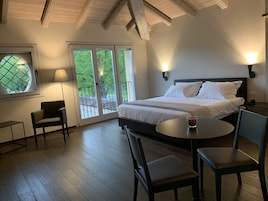 Quarto com uma cama grande, uma escrivaninha, uma cadeira, uma mesa e uma janela com vista para árvores.