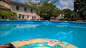 Piscina com um mural colorido na borda, rodeada por um edifício com telhado em azulejos e janelas.