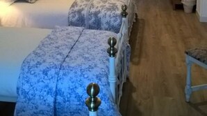 Quarto com duas camas, piso de madeira, luminária pendente, ventilador e porta para um banheiro.