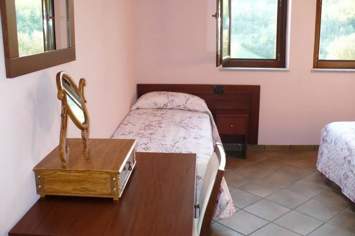 Quarto com cama, cómoda de madeira, espelho e janela.