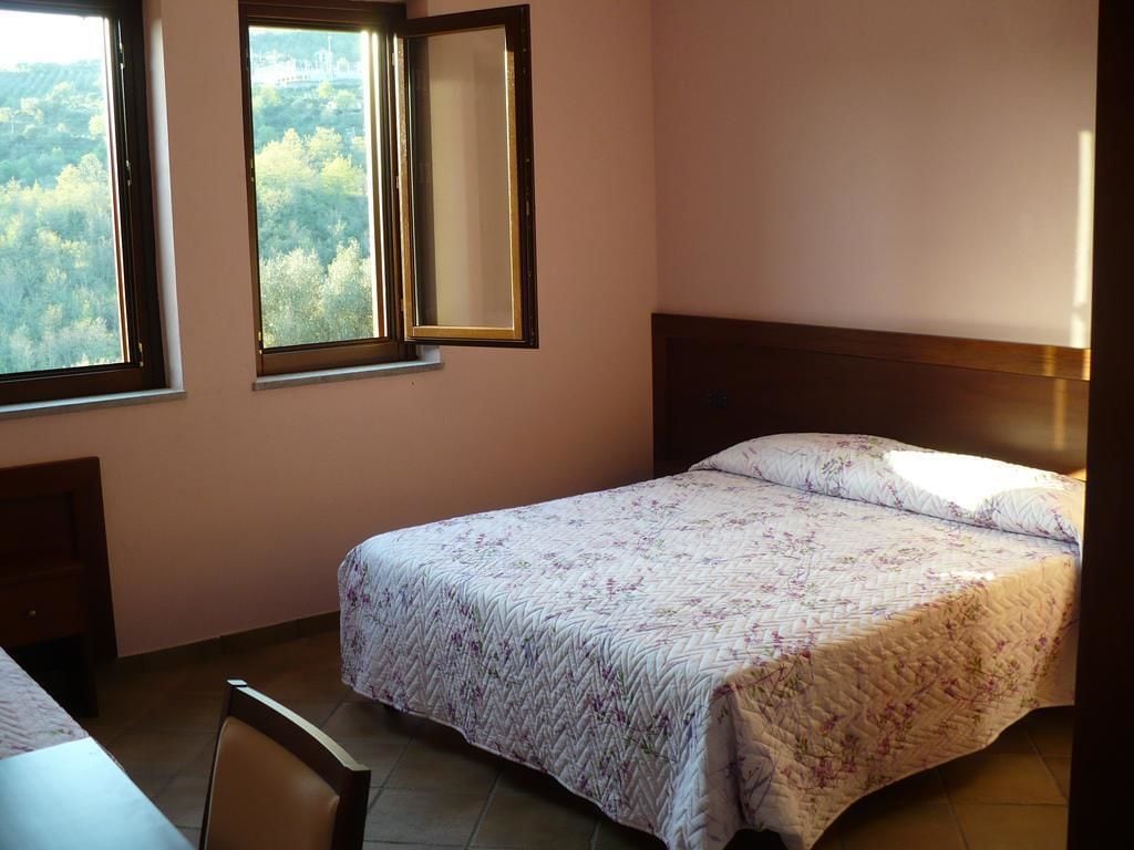Quarto com cama, duas janelas e vista para o verde.