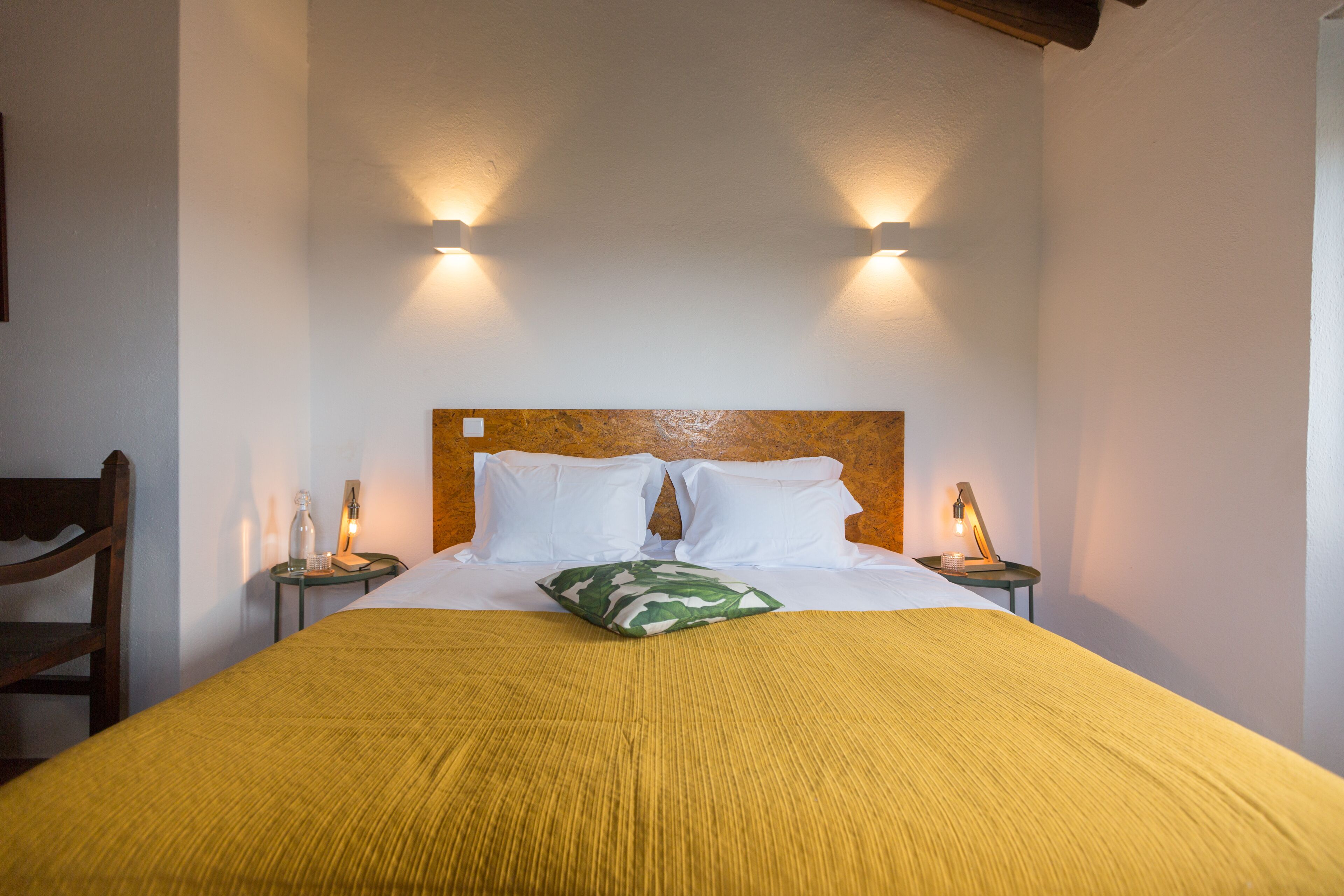 Uma cama bem arrumada com cabeceira de madeira, duas luminárias de apoio e um travesseiro com padrão verde.