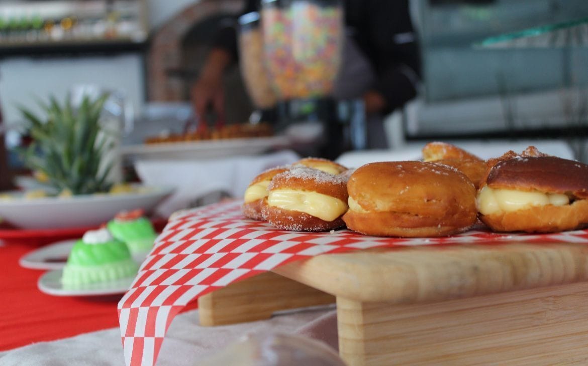 Uma mesa com doces, incluindo donuts e uma sobremesa verde, sobre uma toalha xadrez vermelha e branca.