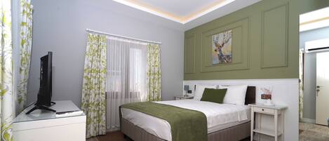 Quarto de hotel com cama, escrivaninha, televisão e janela com cortinas.