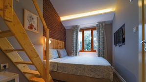 Quarto com cama, escada de madeira, janela com cortinas e televisão fixada na parede.