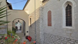 Uma ruela estreita com um edifício de pedra, apresentando uma grande porta em arco e uma janela com grade de metal.