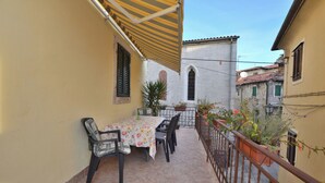 Pequeno pátio externo com mesa e cadeiras, toldo amarelo e plantas em vasos.
