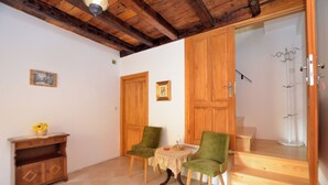 Quarto com piso de madeira, duas cadeiras verdes, uma mesa pequena, um armário de madeira e uma porta para a área do chuveiro.