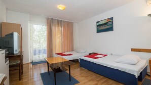 Quarto com duas camas, uma escrivaninha, televisão e janela com cortinas.
