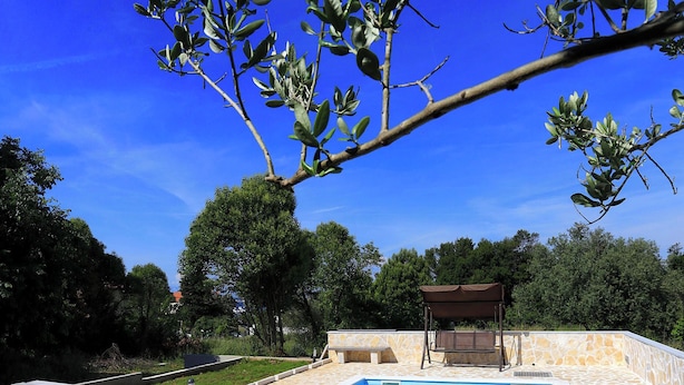Piscina retangular com borda de pedra, rodeada por um muro de pedra e uma área gramada.