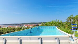 Piscina ao ar livre com vista para uma cidade costeira e colinas ao fundo.