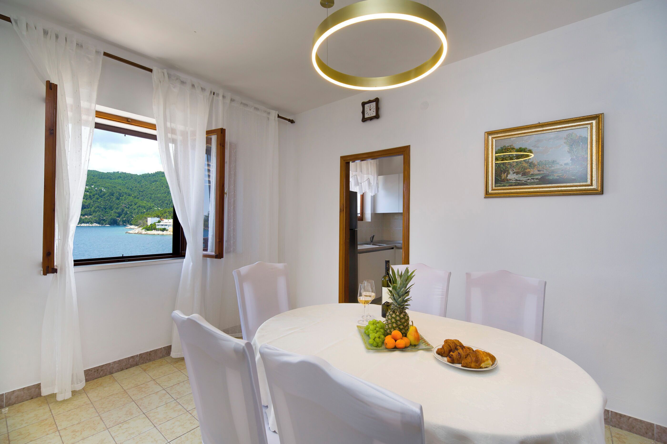 Uma área de refeições com uma mesa posta para dois, com um prato de frutas e uma garrafa de vinho.