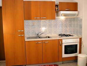 Cozinha com armários de madeira, pia de aço inoxidável, fogão a gás e forno embutido.