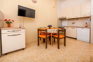 Uma cozinha compacta com mesa de jantar, cadeiras, televisão e um pequeno armário.