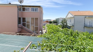 Um edifício residencial com telhado inclinado, antena parabólica e área de jardim com folhagem verde.