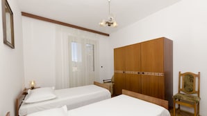 Quarto com duas camas de solteiro, guarda-roupa de madeira, uma cadeira e mesa de cabeceira com luminária.