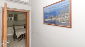 Um corredor com área de jantar, uma pintura emoldurada de paisagem costeira e um aparelho de ar condicionado.