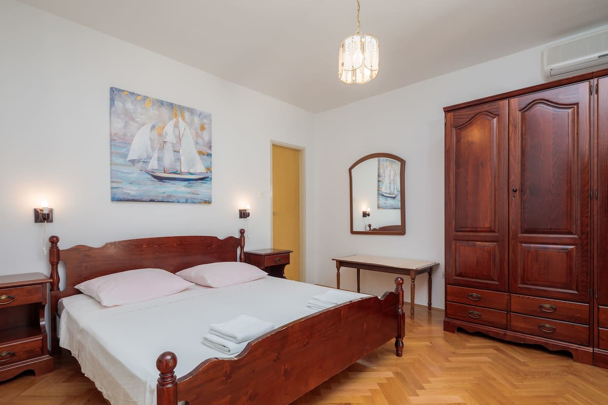 Quarto com cama de madeira, mesas de cabeceira, cômoda, quadro de um veleiro e espelho.