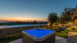 Uma banheira de hidromassagem em um quintal com uma parede de pedra, piscina e vista para o pôr do sol.