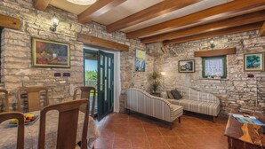 Um quarto rústico com paredes de pedra, uma mesa de jantar, cadeiras, um sofá listrado e teto de madeira.