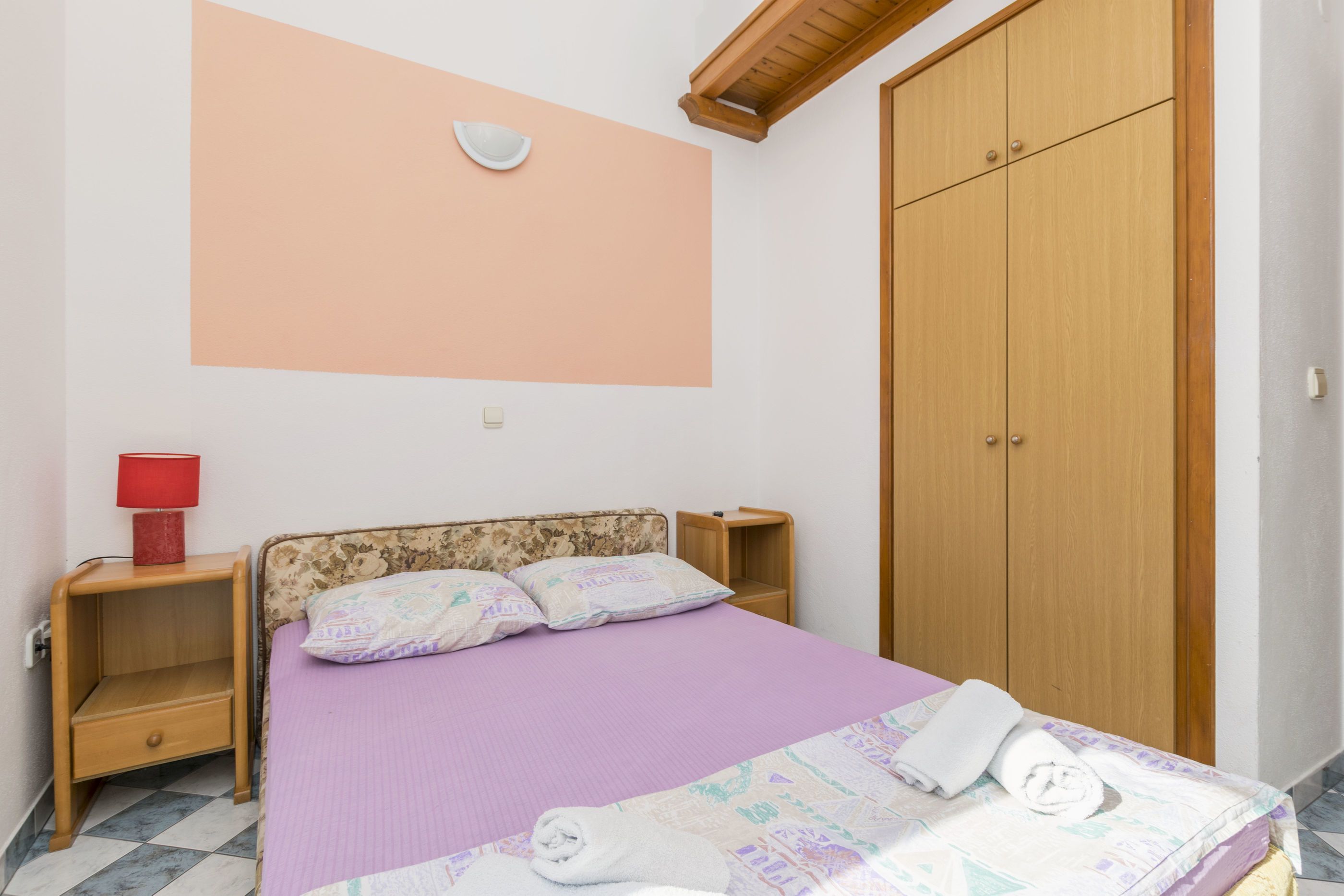 Quarto com cama, mesa de cabeceira com luminária, guarda-roupa e luminária na parede.