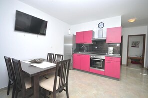 Uma cozinha moderna com armários rosa, uma geladeira de aço inoxidável, forno embutido e uma TV de tela plana na parede.