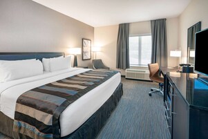 Quarto de hotel com uma cama grande, escrivaninha, cadeira, televisão e janela com cortinas.
