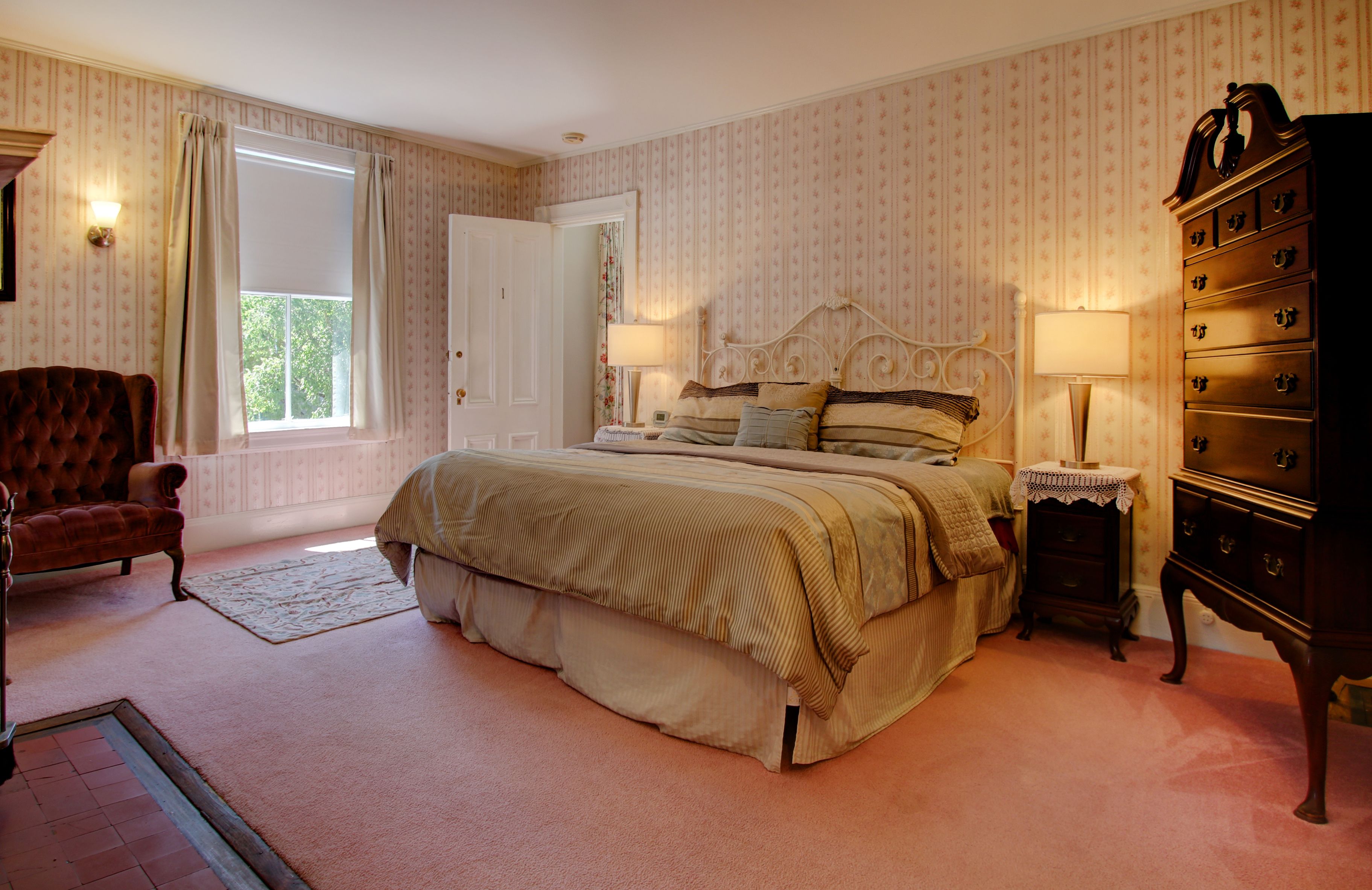 Um quarto com uma cama grande, cômoda, cadeira e janela com cortinas.