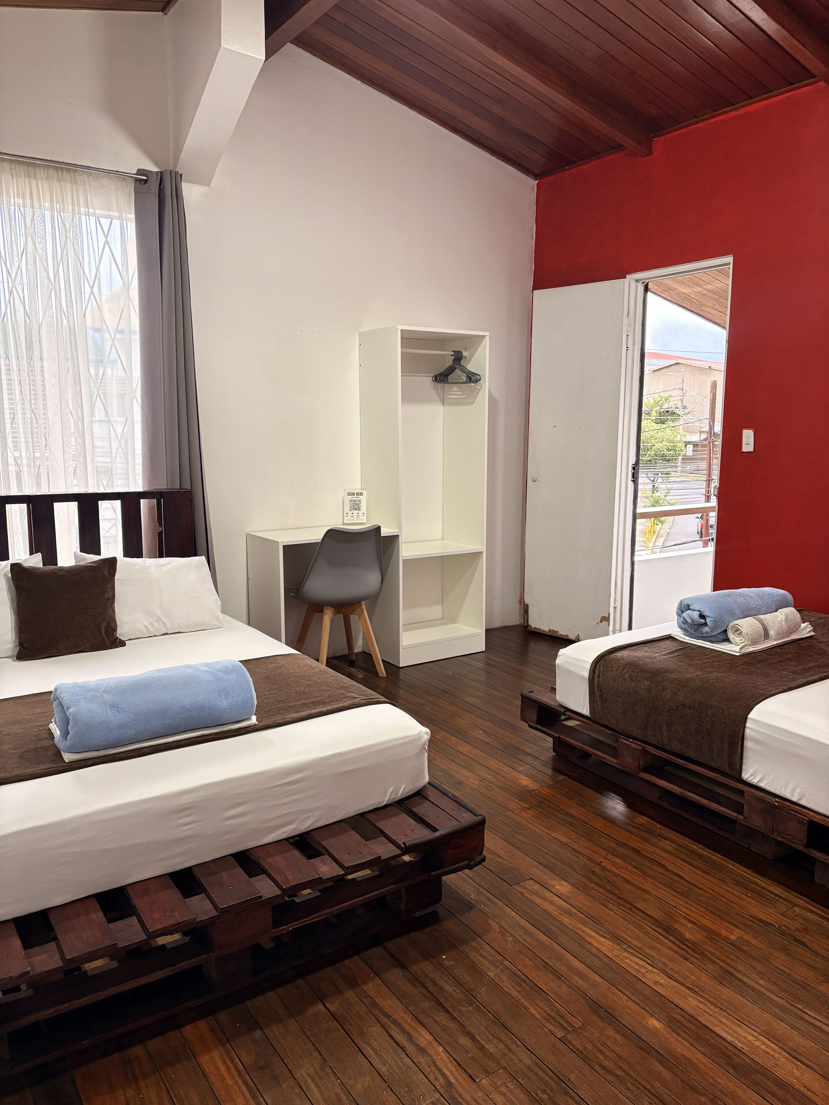 Quarto com duas camas, uma escrivaninha, um guarda-roupa e vista por uma porta aberta.