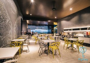 Um restaurante com cadeiras e mesas amarelas, uma parede grande com lousa e vista para a cidade.