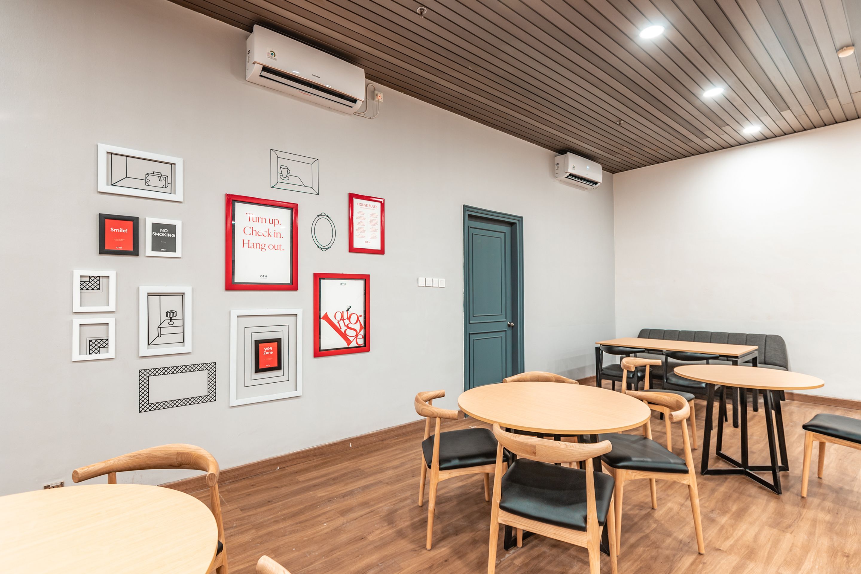 Uma sala de reuniões moderna com mesas e cadeiras de madeira, uma porta verde-água e diversas obras de arte emolduradas nas paredes.