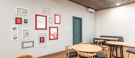 Uma sala de reuniões moderna com mesas e cadeiras de madeira, uma porta verde-água e diversas obras de arte emolduradas nas paredes.