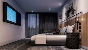 Quarto moderno com cama, televisão na parede, mesa pequena e uma cadeira.